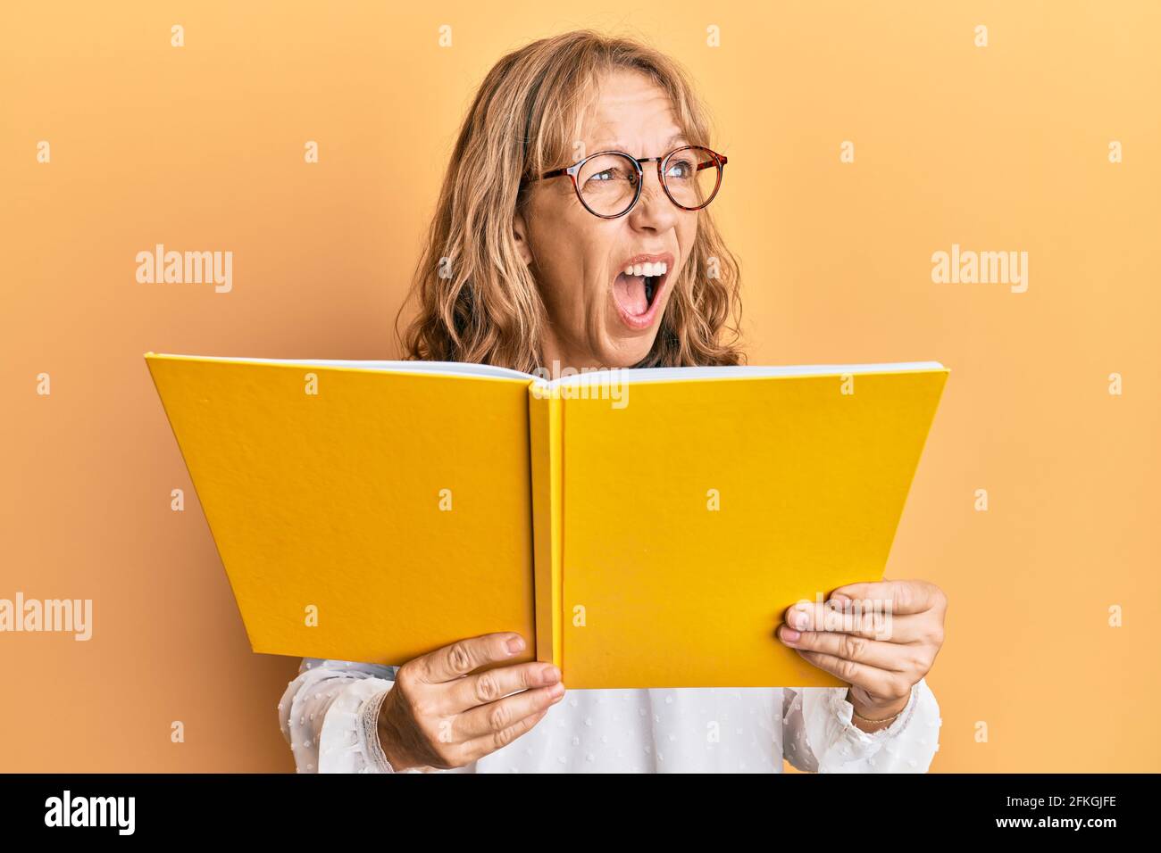Middle age blonde woman reading a book wearing glasses angry and mad ...