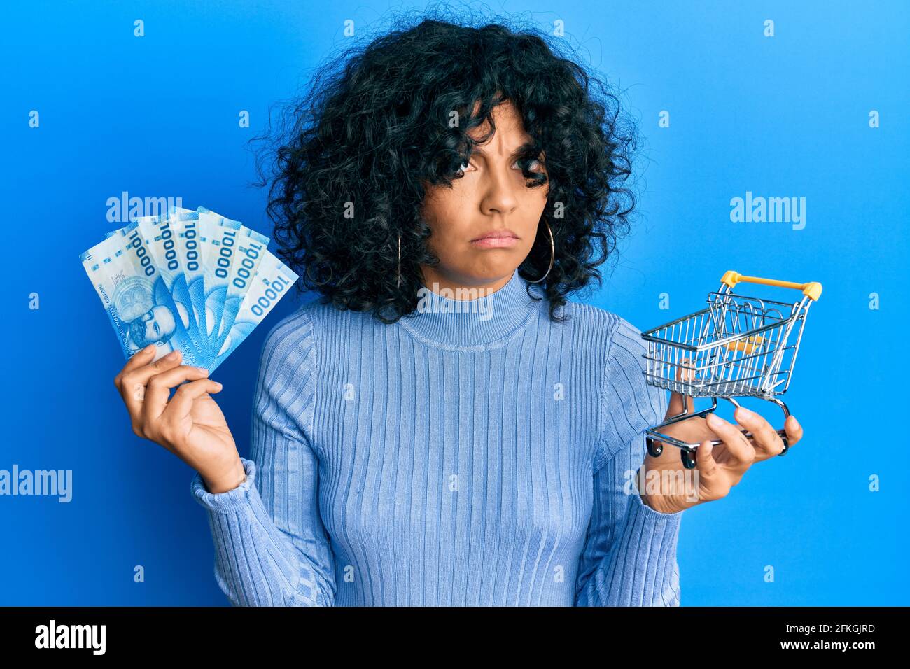 Young hispanic woman holding small supermarket shopping cart and ...