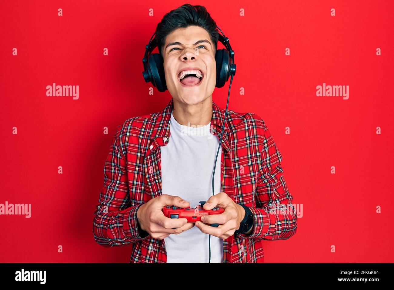Young hispanic man playing video game holding controller angry and mad ...