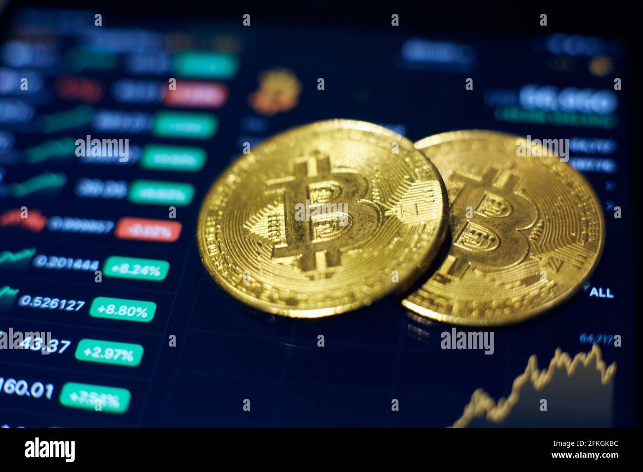 Two gold bitcoin coins lie on the tablet screen, which shows indicators ...