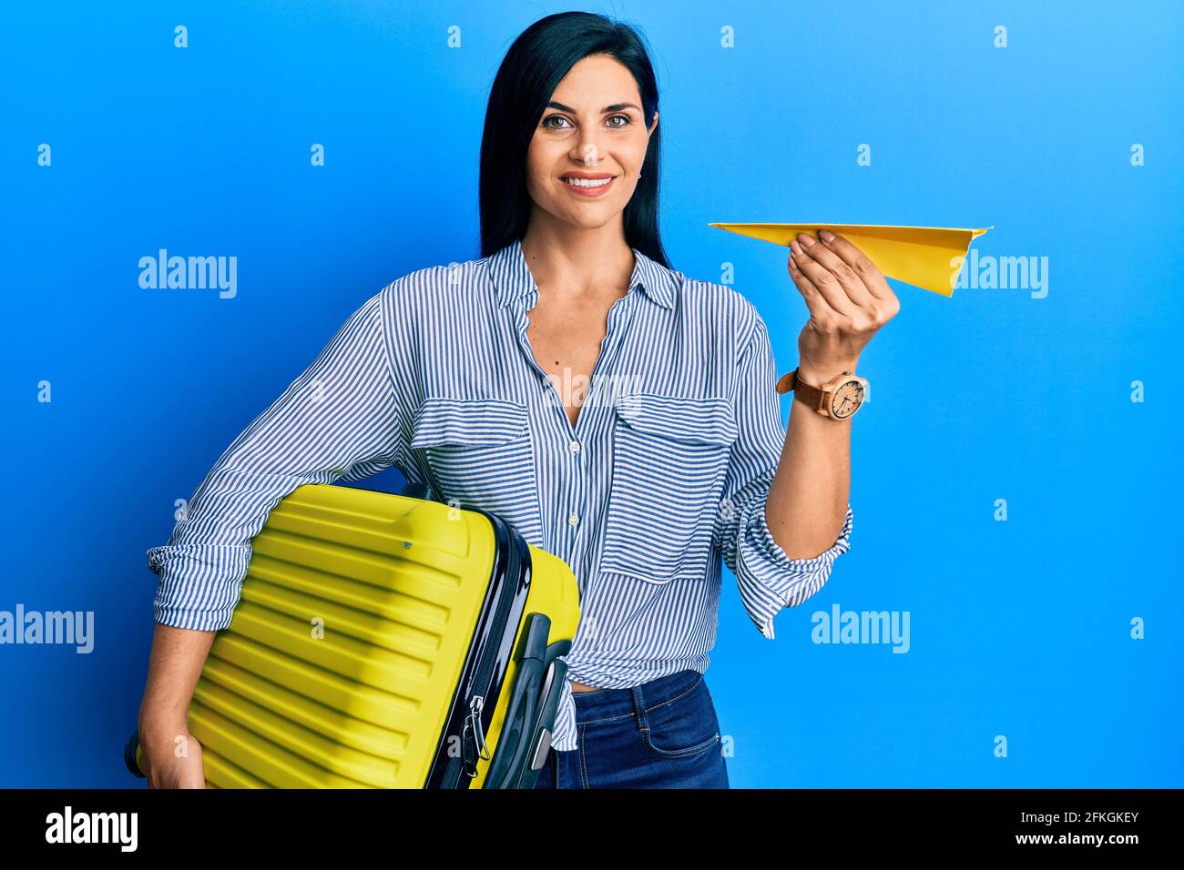 Young caucasian woman holding cabin bag and paper airplane smiling with ...