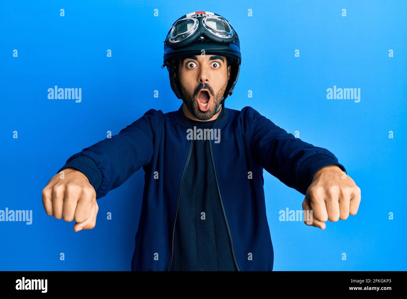 Young hispanic man holding motorcycle helmet afraid and shocked with ...