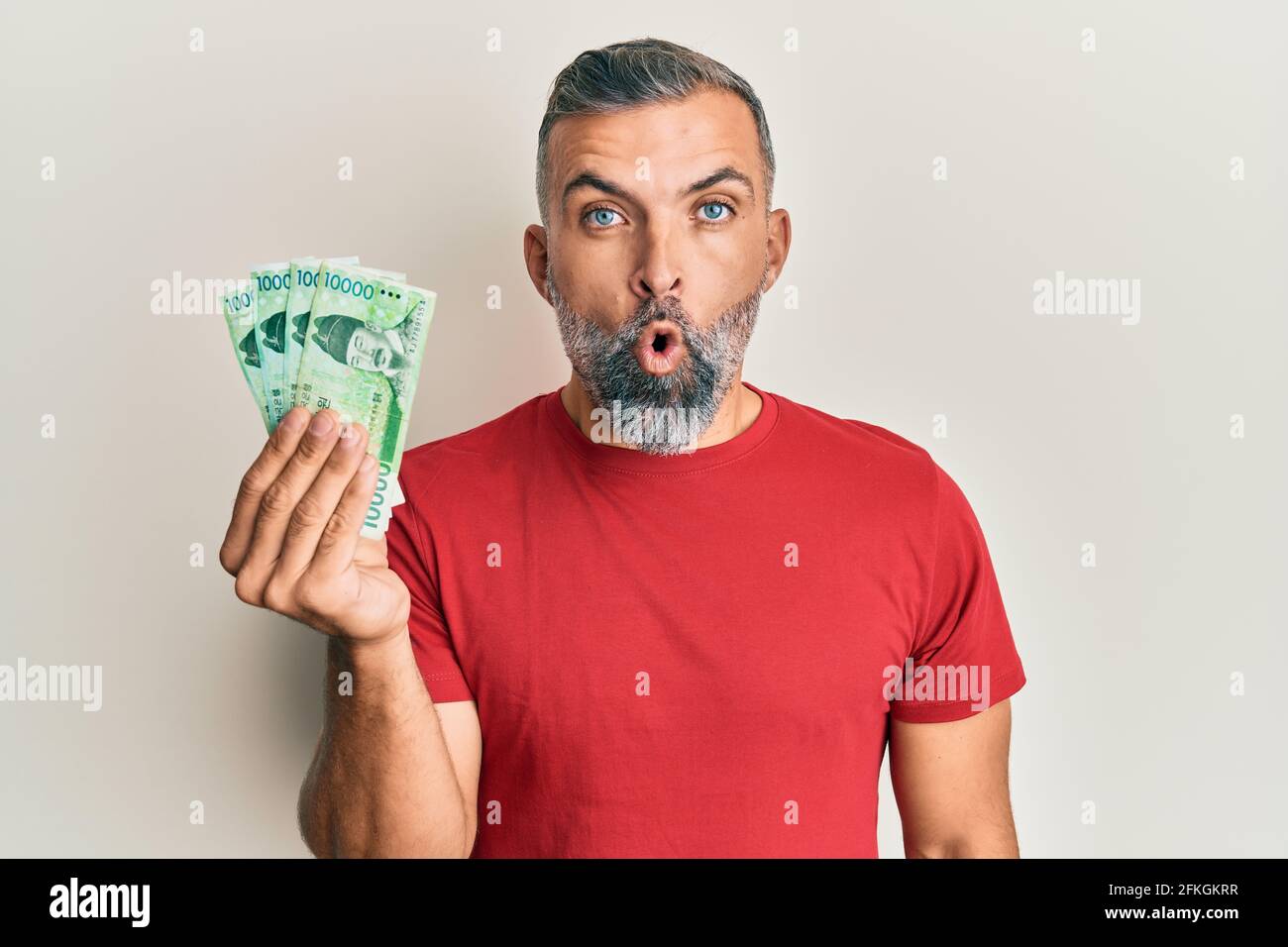 Middle age handsome man holding 10000 south korean won banknotes scared ...