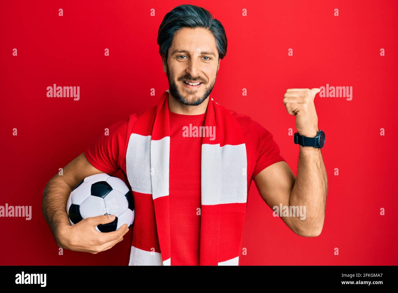 Young hispanic man football hooligan holding ball pointing thumb up to ...
