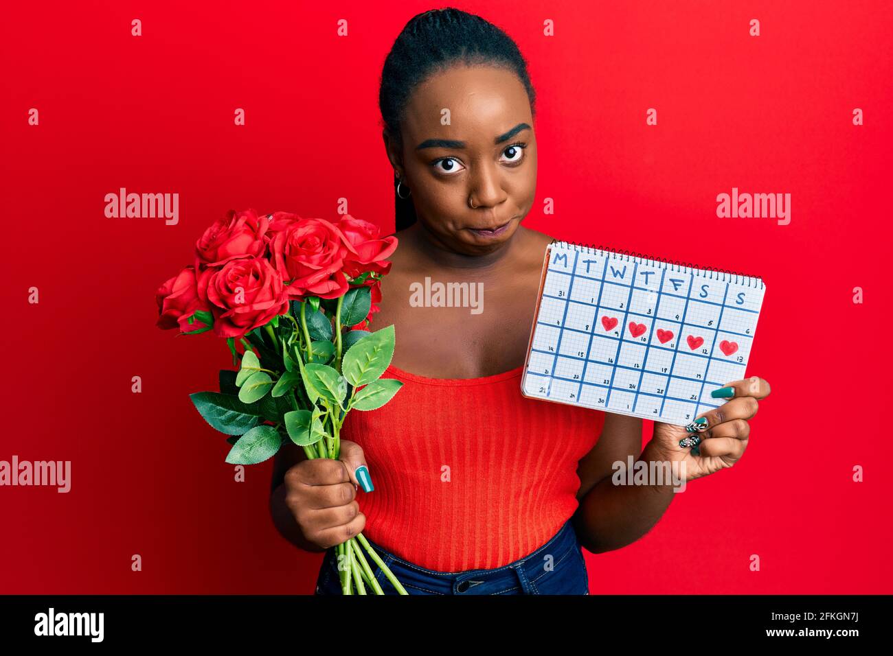 Young african american woman holding heart calendar and flowers skeptic ...