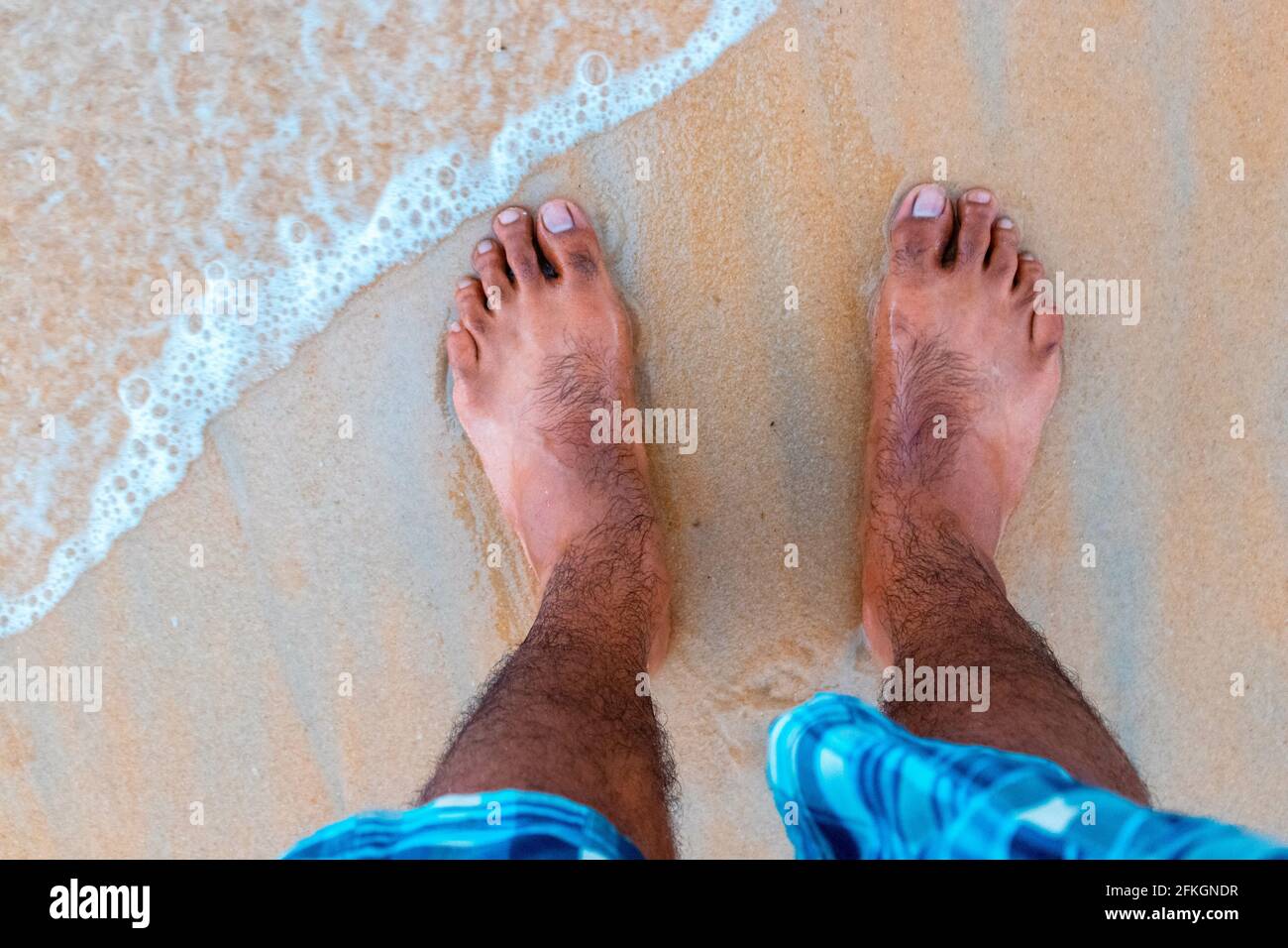 Top view shot of man's feet on the sea sand with bubble float wave ...
