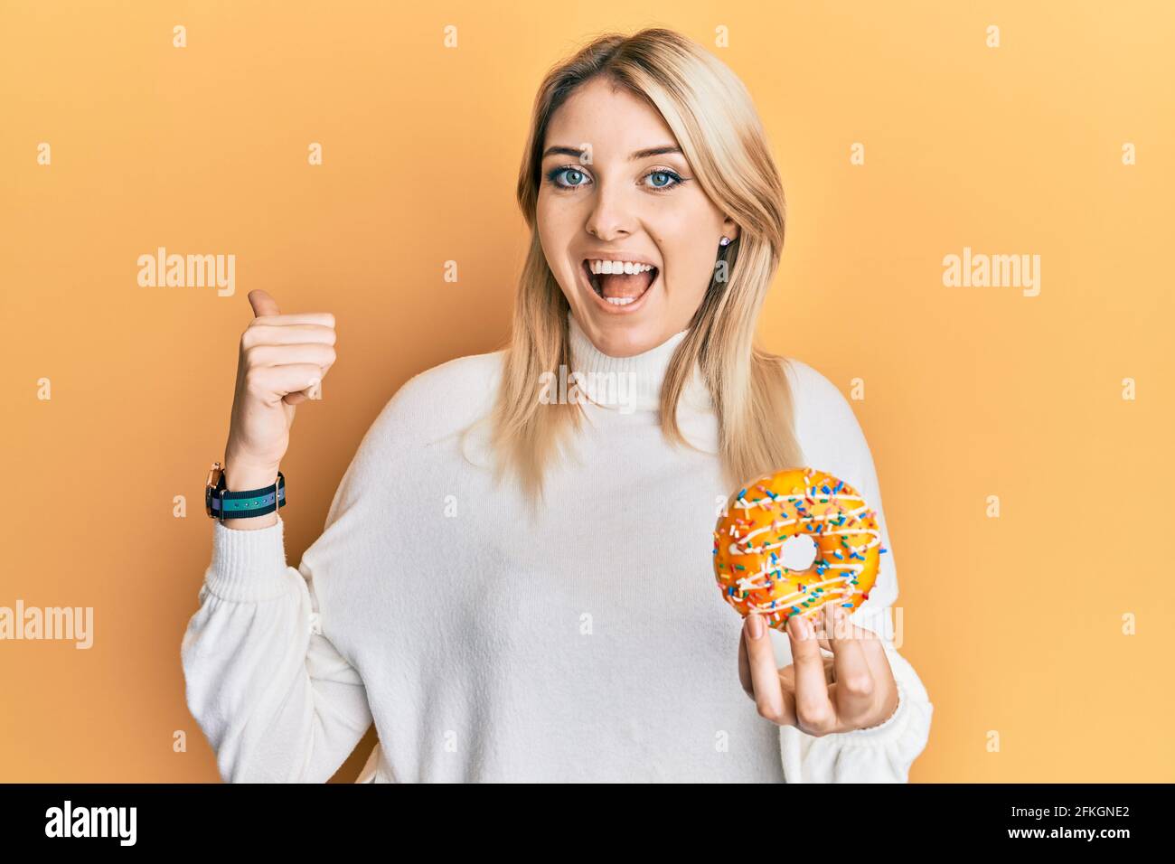 Young caucasian woman holding donut pointing thumb up to the side ...