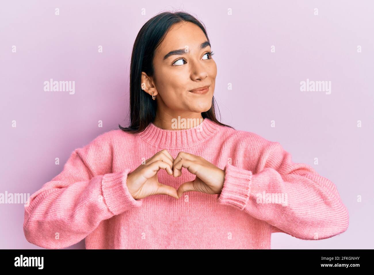 Young asian woman doing heart symbol with hands smiling looking to the ...