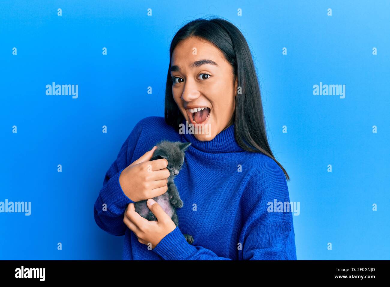Young hispanic girl with surprised face holding cute cat over isolated ...