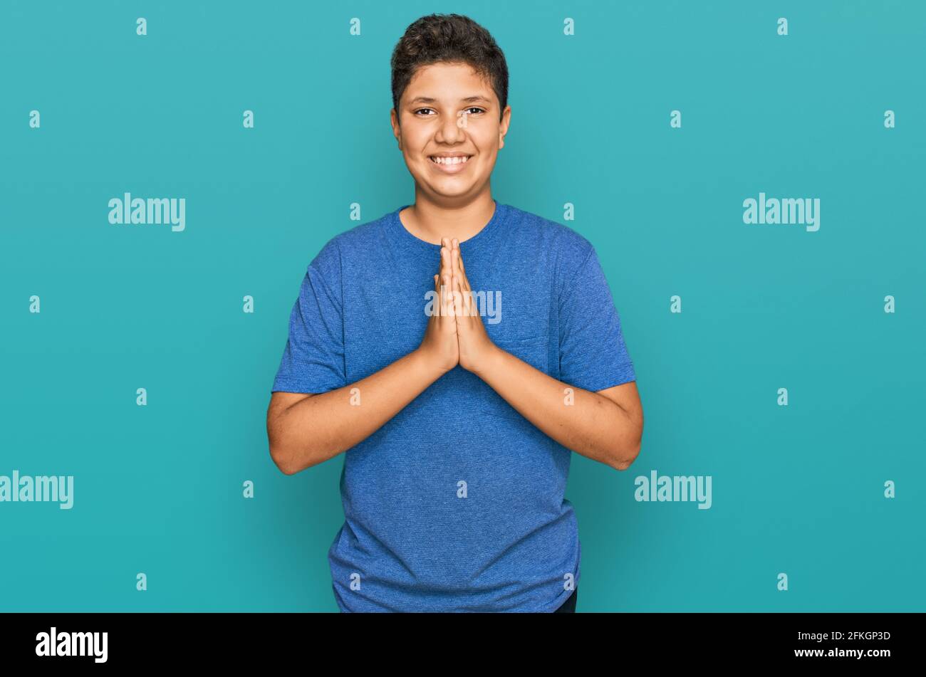 Teenager hispanic boy wearing casual clothes praying with hands ...