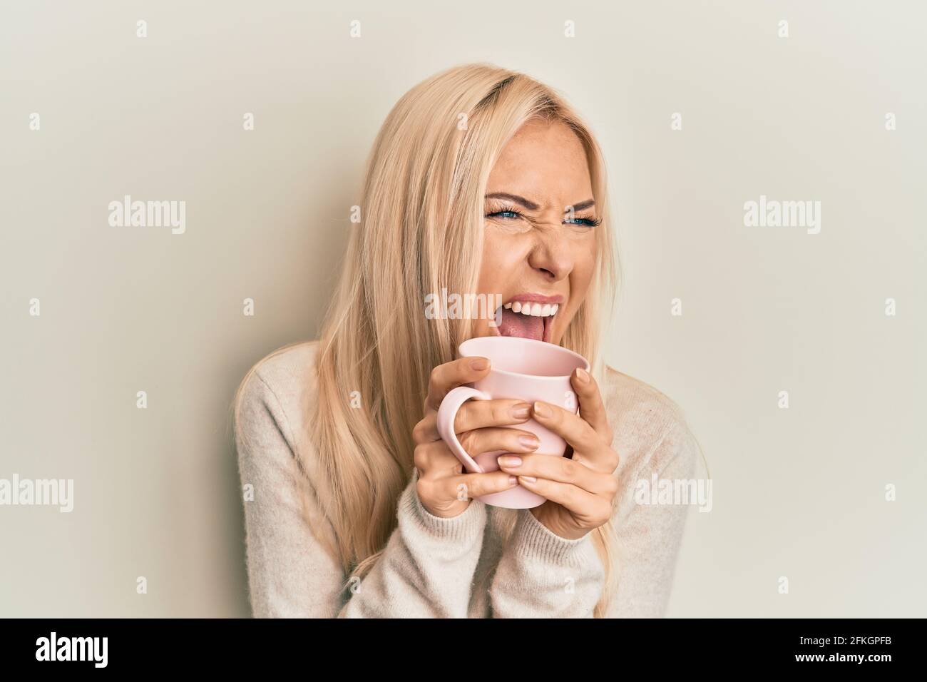 Young blonde woman drinking a cup of coffee angry and mad screaming ...
