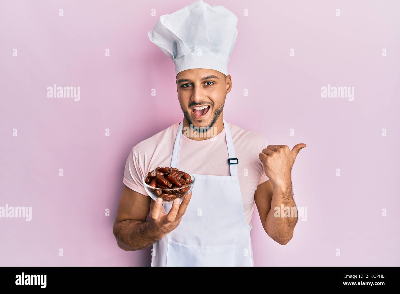 Young arab man wearing professional cook uniform holding bowl with ...