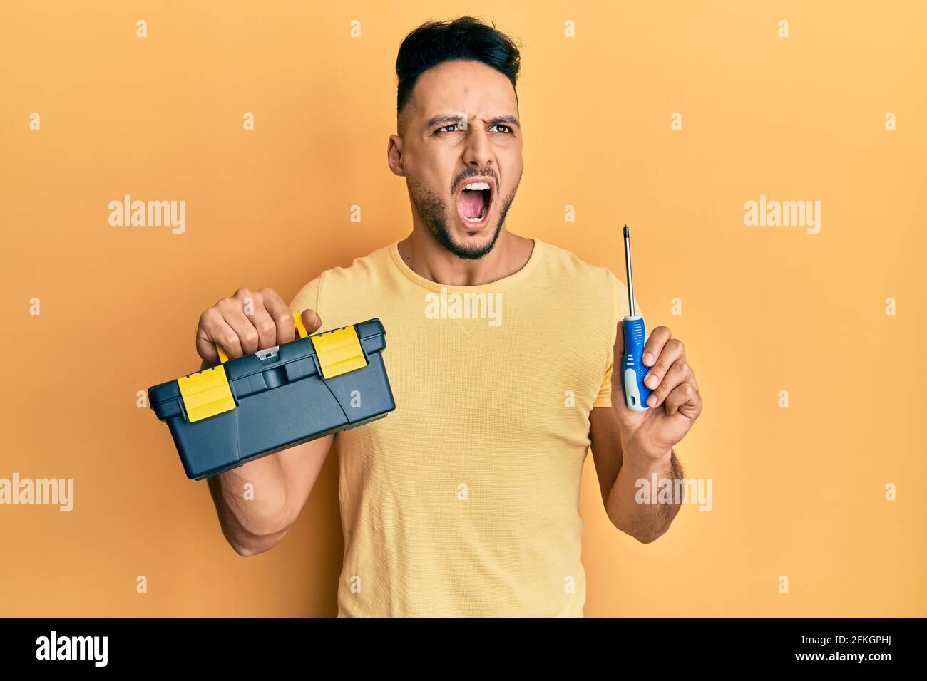 Young arab man holding toolbox and screwdriver angry and mad screaming ...