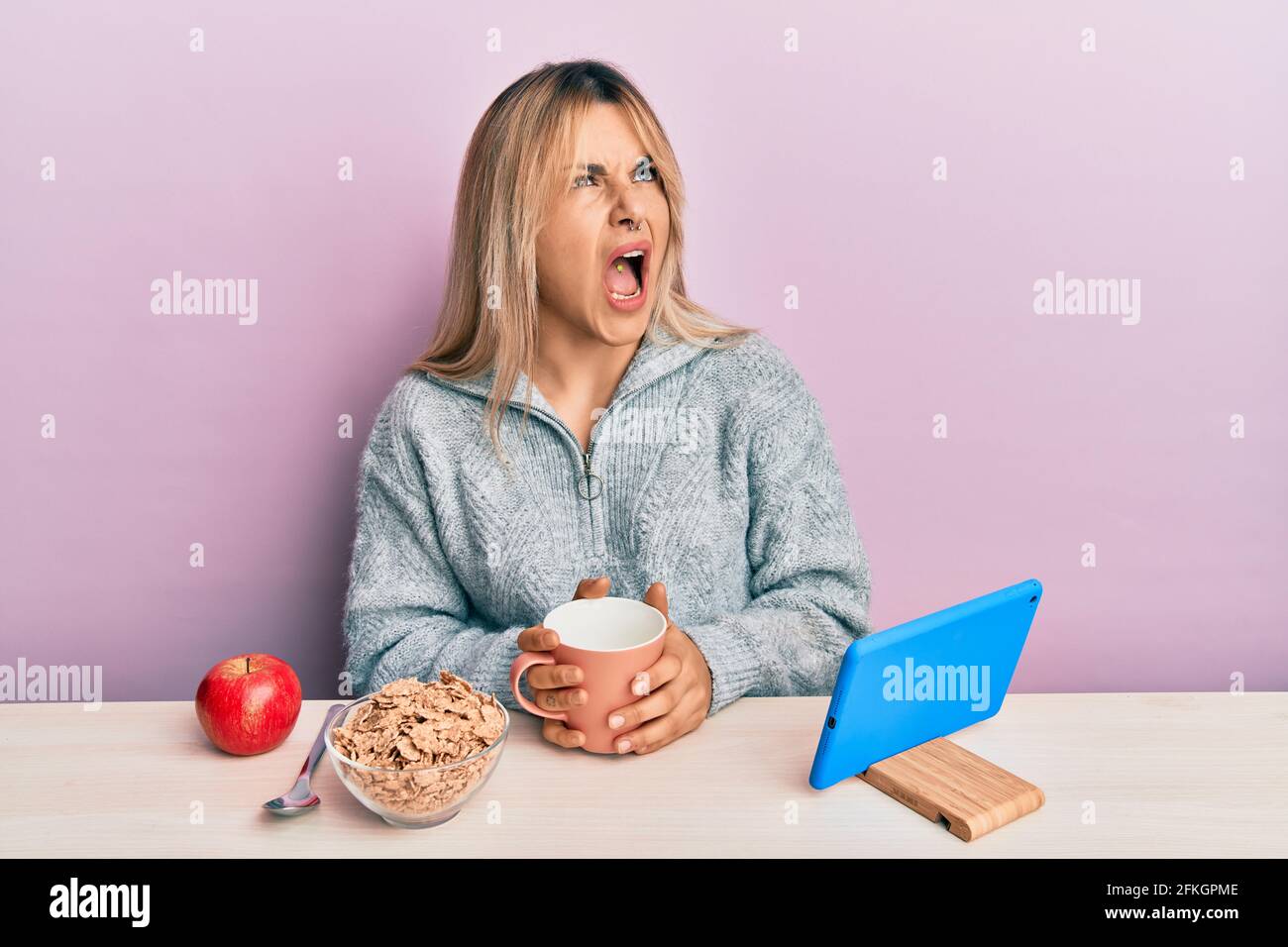 Young caucasian woman having breakfast looking at the tablet sitting on ...