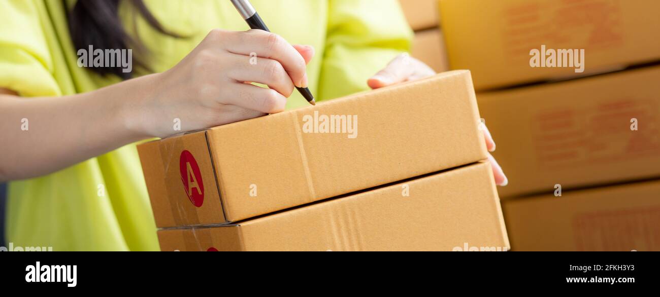 Closeup hand of young asian woman writing address on parcel box at home ...