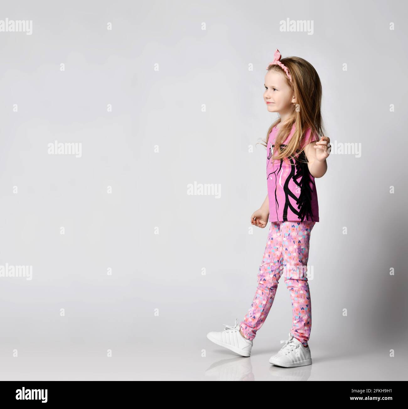 Happy frolic blonde kid girl in summer clothing colorful pants and t ...