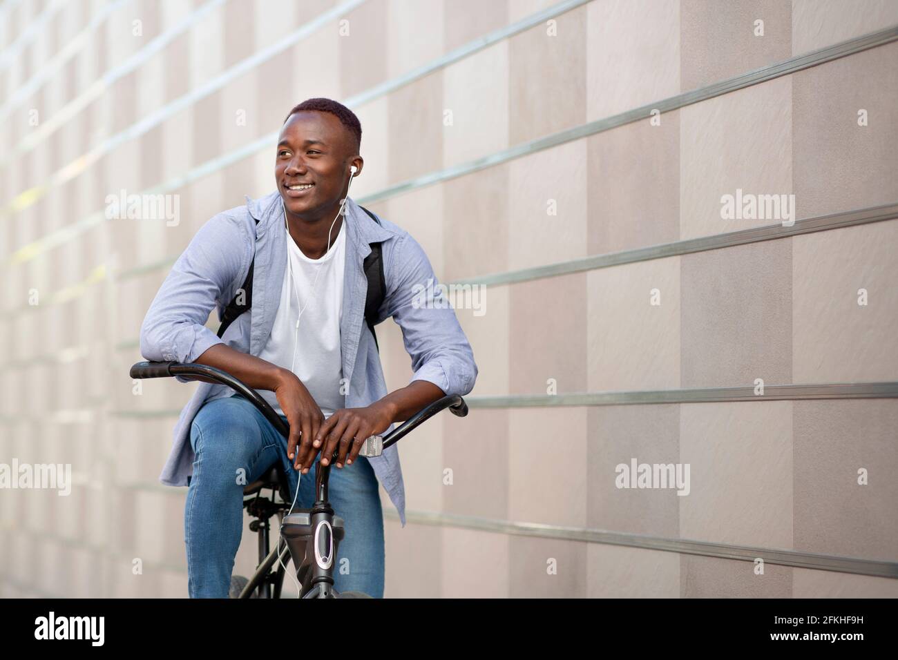 Happy African American man listening to music while riding bike near ...