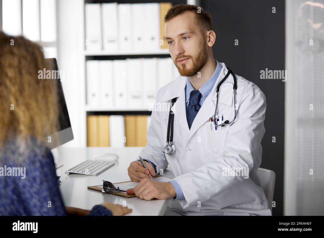 Friendly red-bearded doctor and patient woman discussing current health ...