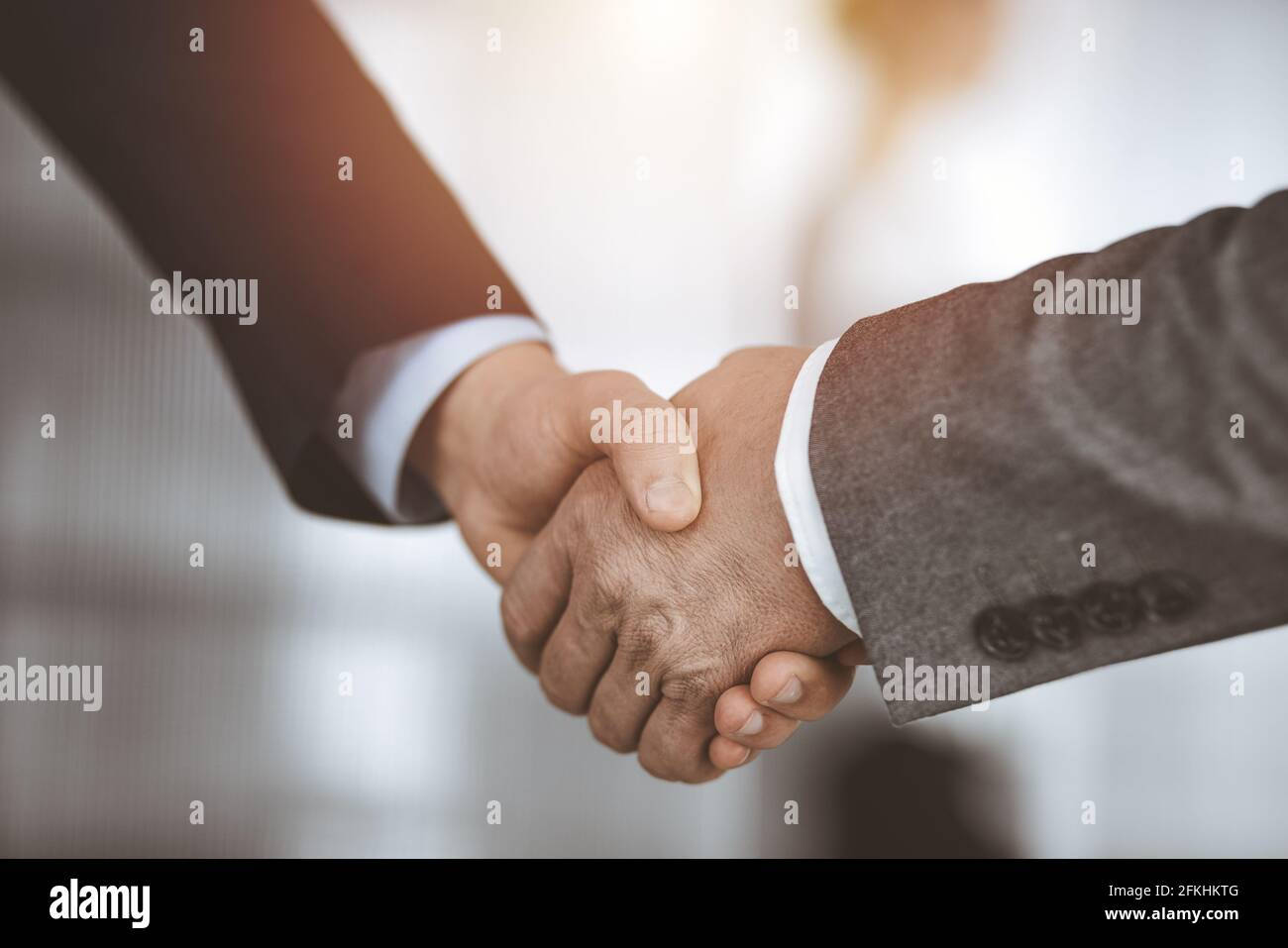 Business people standing and shaking hands in sunny office, close-up ...