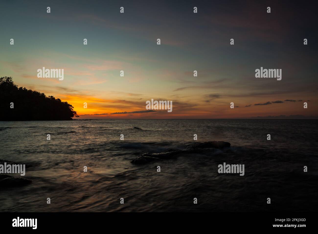 Vivid sunset sky waterscape and silhouette forest island background ...