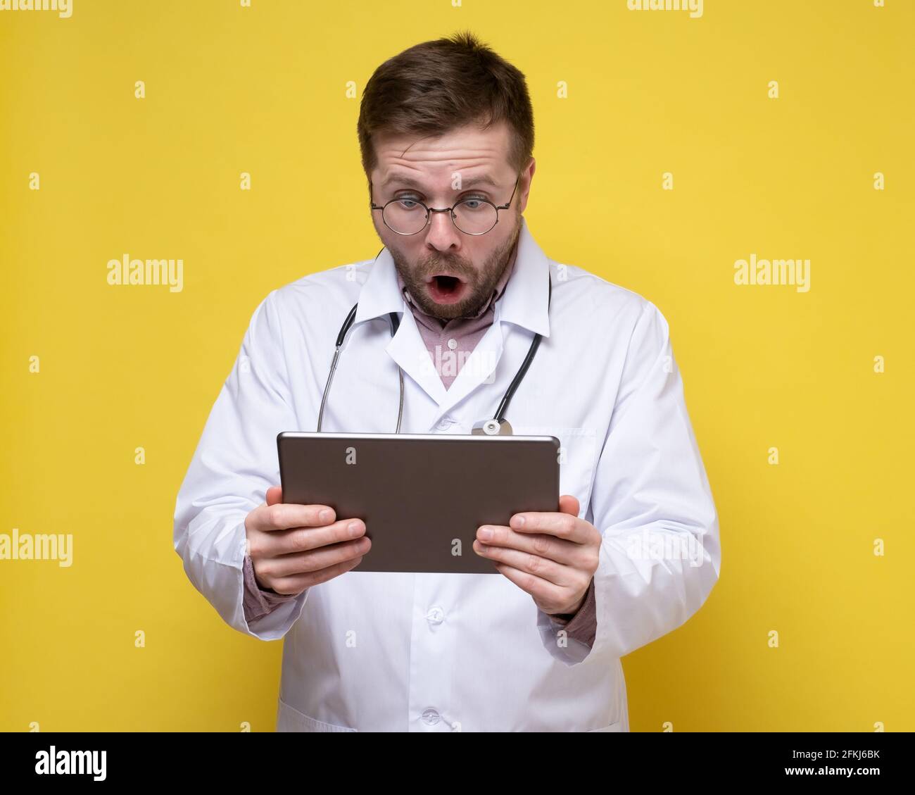 Frightened, shocked doctor looks at a tablet with an open mouth and big ...