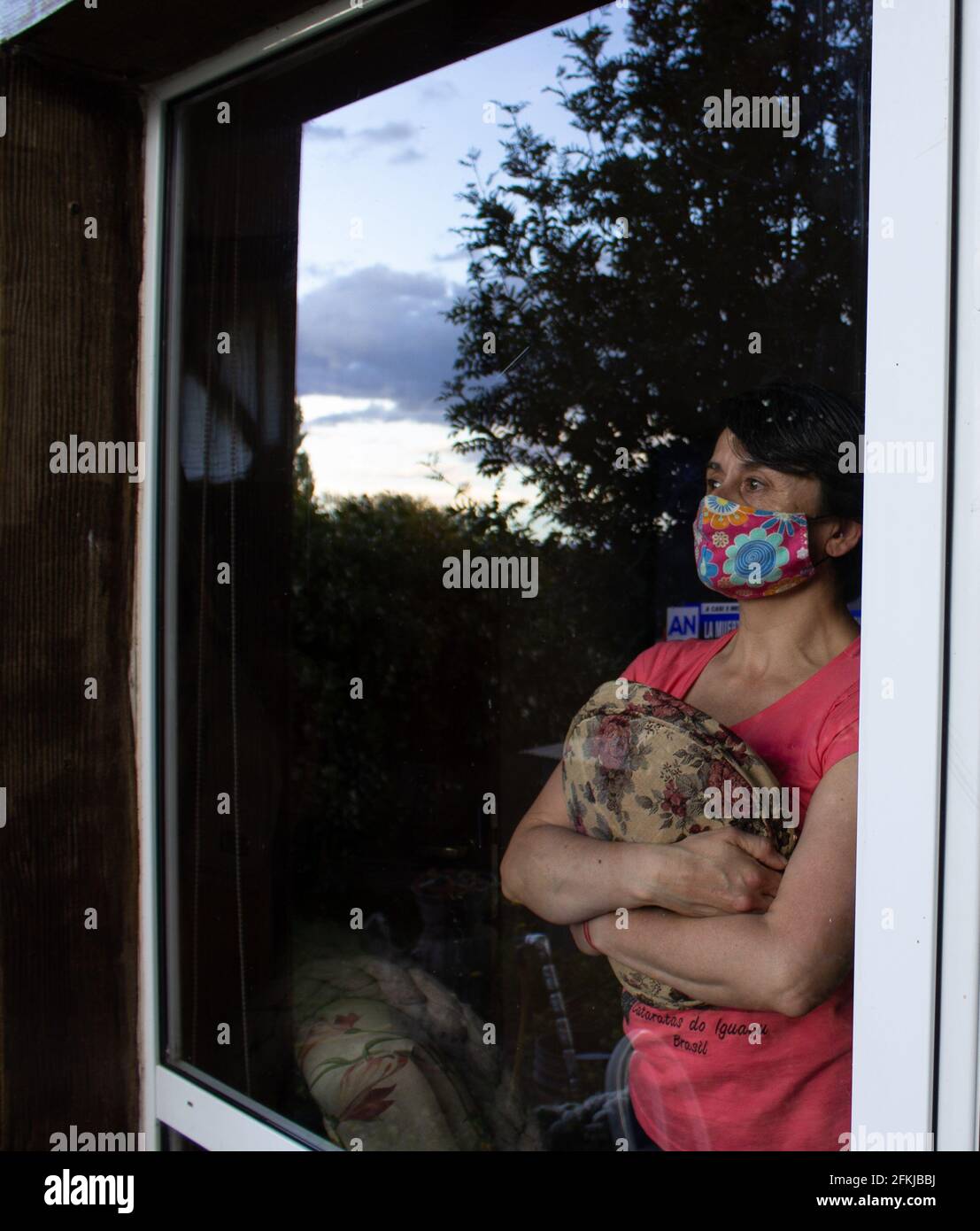 A sad caucasian woman standing by the window with the mask on during ...