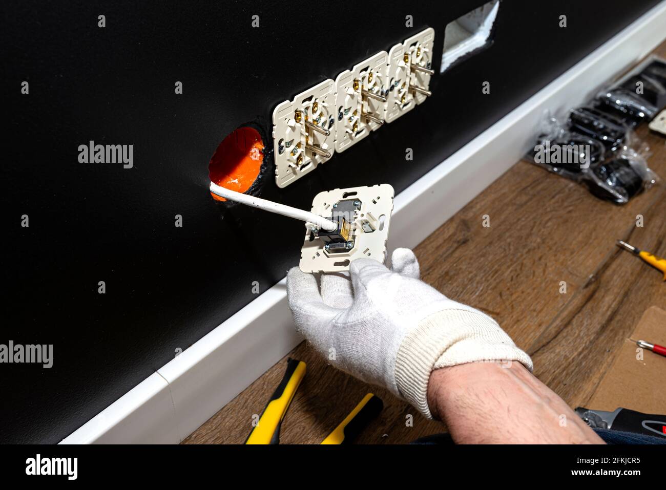 An electrician in white gloves is installing a TV socket and satellite ...