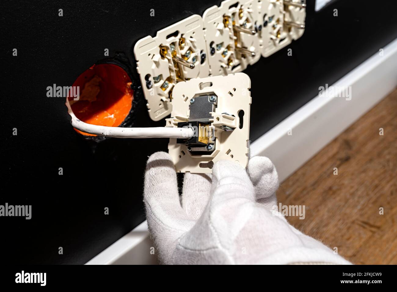 An electrician in white gloves is installing a TV socket and satellite ...