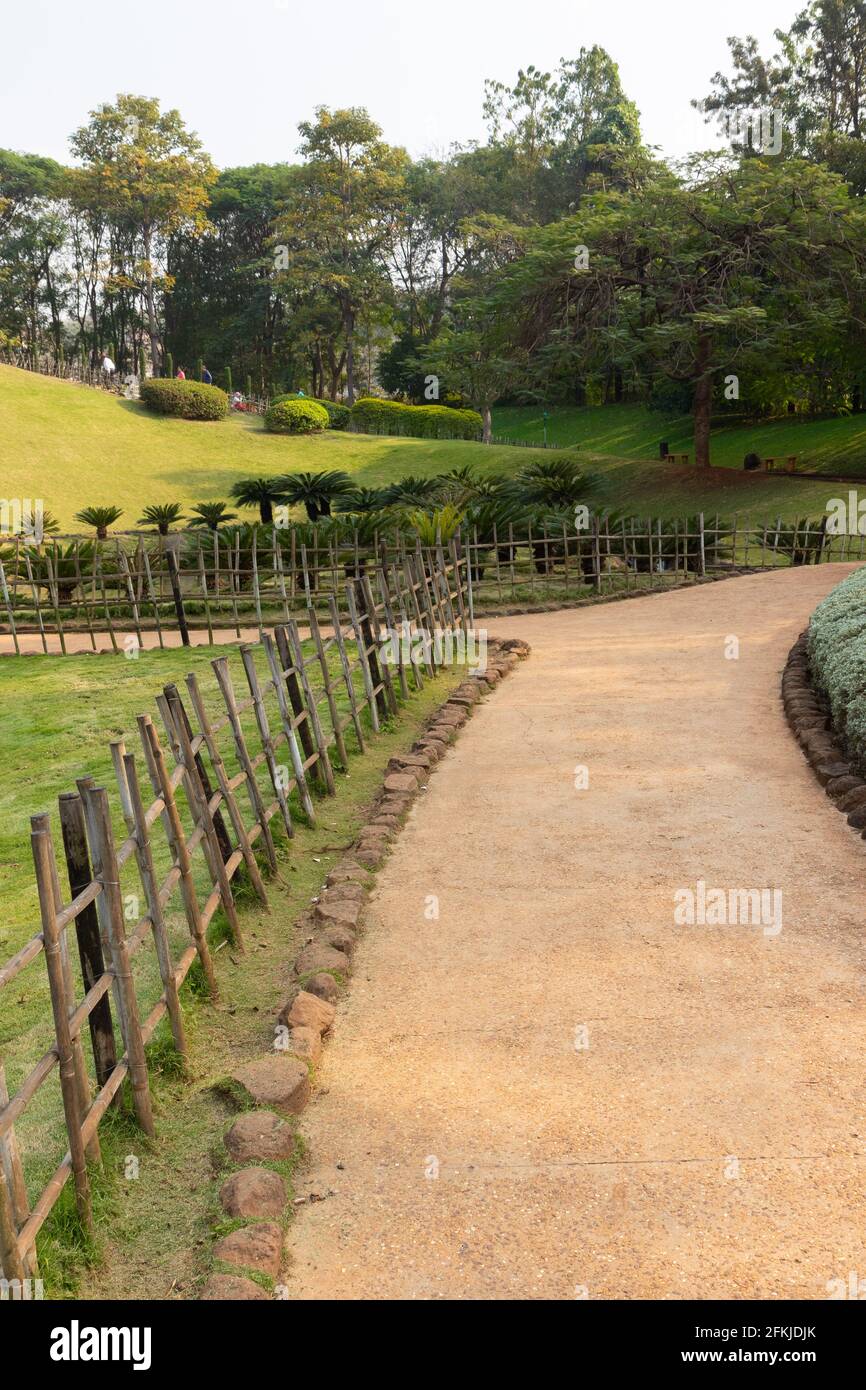 A walkway in a park with fence on one side and and greenery all around ...