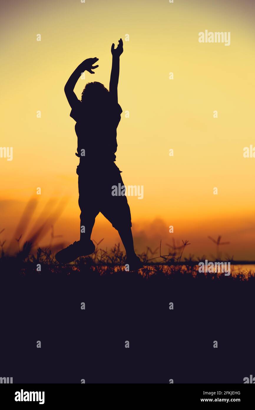 Silhouette back view of child jumping against sunset. Boy enjoying the ...