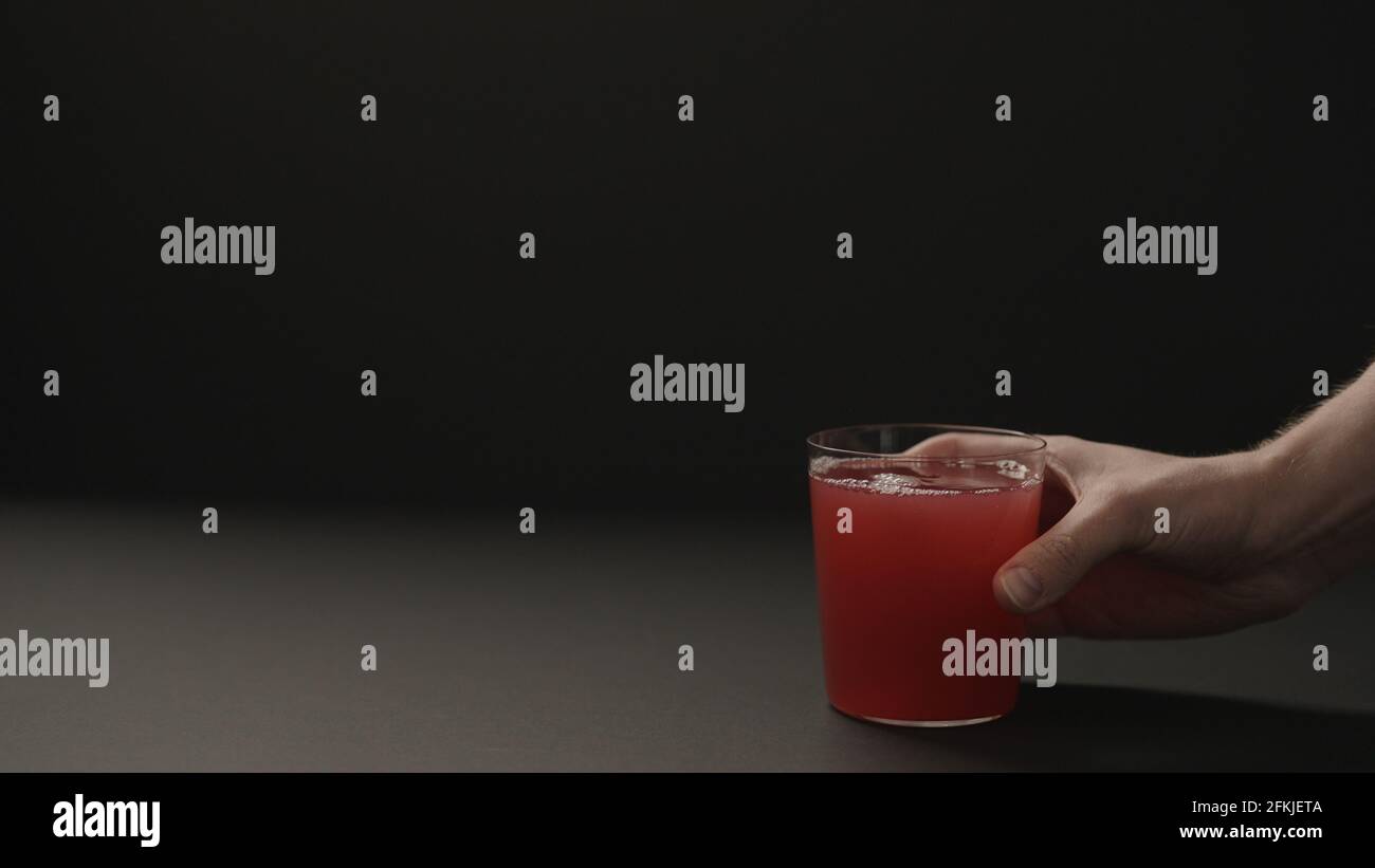 man hand take berry drink in tumbler glass on black paper background ...