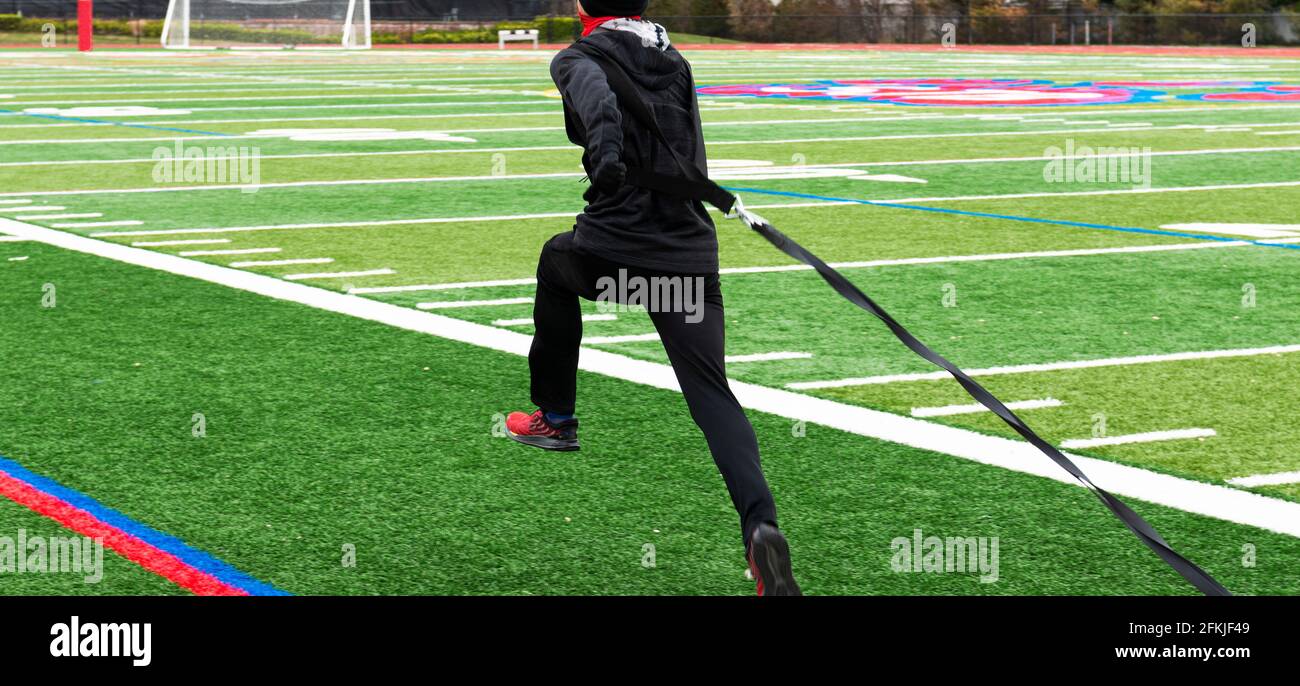 Rear view of a high school boy running while pulling a sled carrying weights during strength and ...