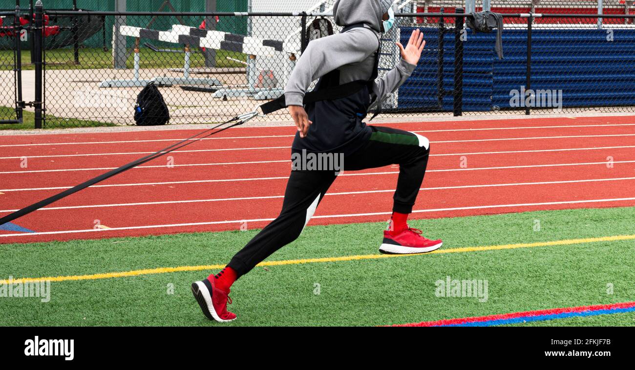 A male high school runner is dragging a sled with weight across a green ...