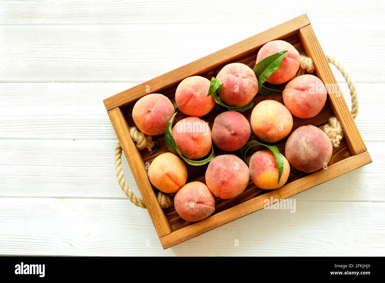 Bunch of ripe organic peaches in pile on wooden tray tray with rope ...