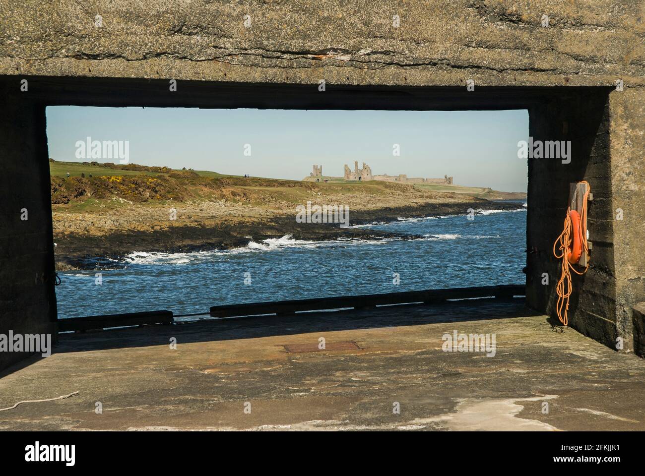 Dunstanburgh castle through a hole in the harbour wall Stock Photo - Alamy