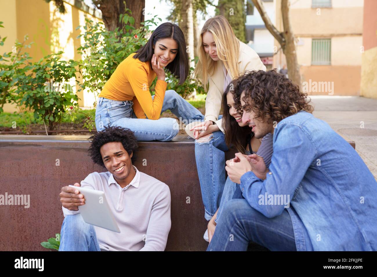Multi-ethnic group of young people looking at a digital tablet outdoors ...