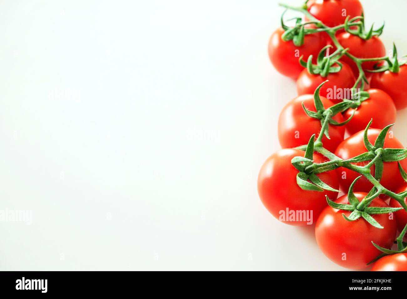 Branch of juicy organic red cherry tomatoes arranged in row on isolated white background ...