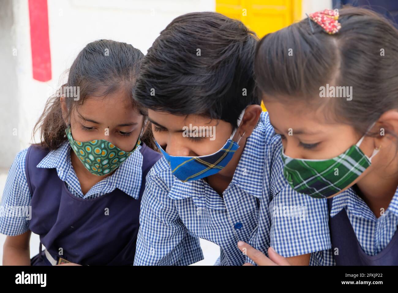 A group of Indian children in face masks and school uniforms using a ...