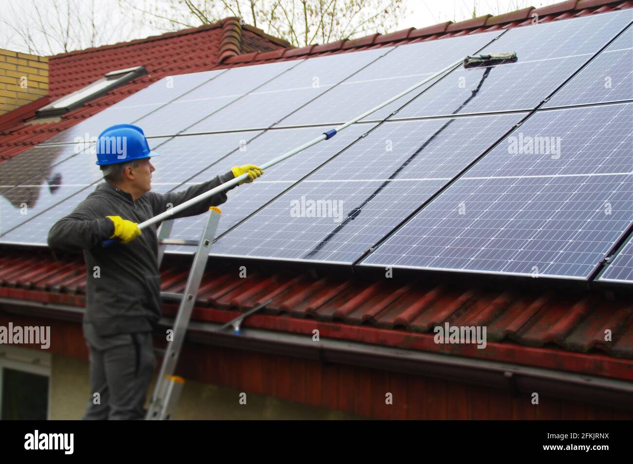 Cleaning solar panels. A man on a ladder cleans and washing a ...