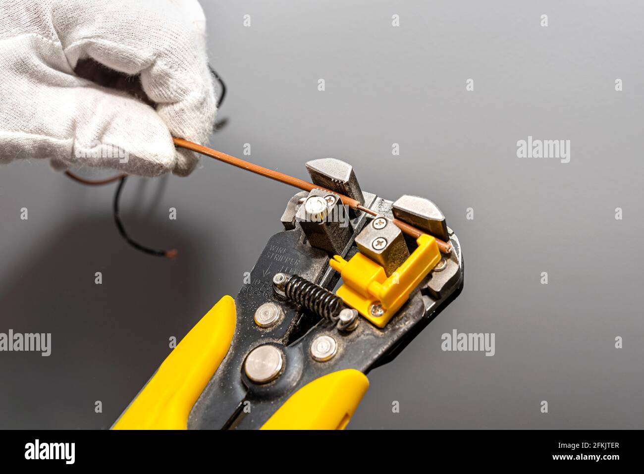 An electrician uses a automatic insulation stripper to prepare the ...