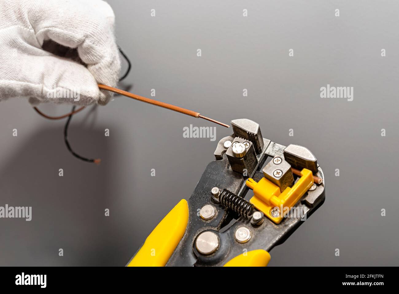 An electrician uses a automatic insulation stripper to prepare the ...
