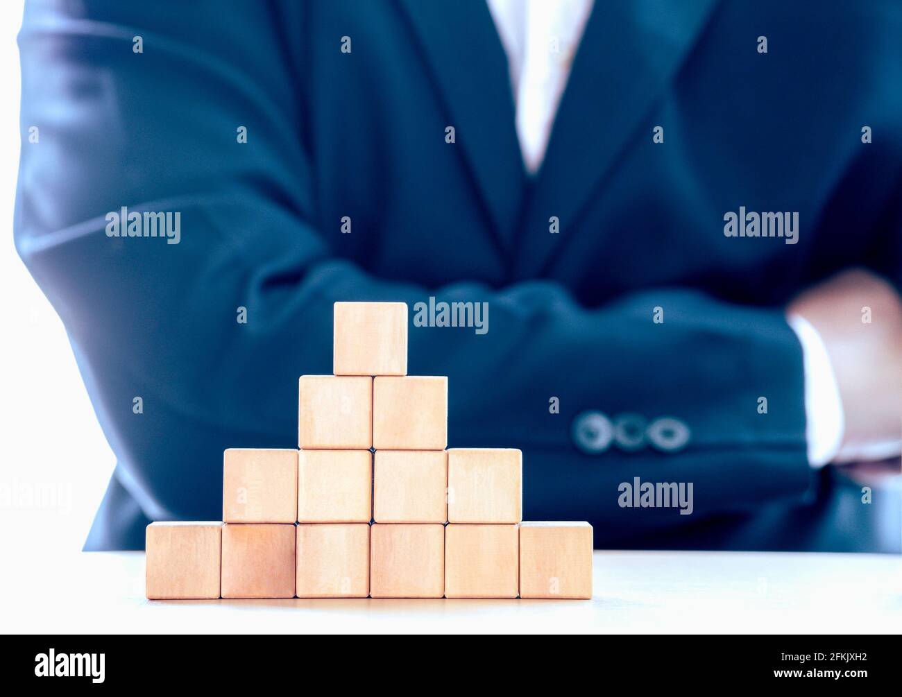 Arranging empty wood cube stacking as pyramid against crossed arms ...