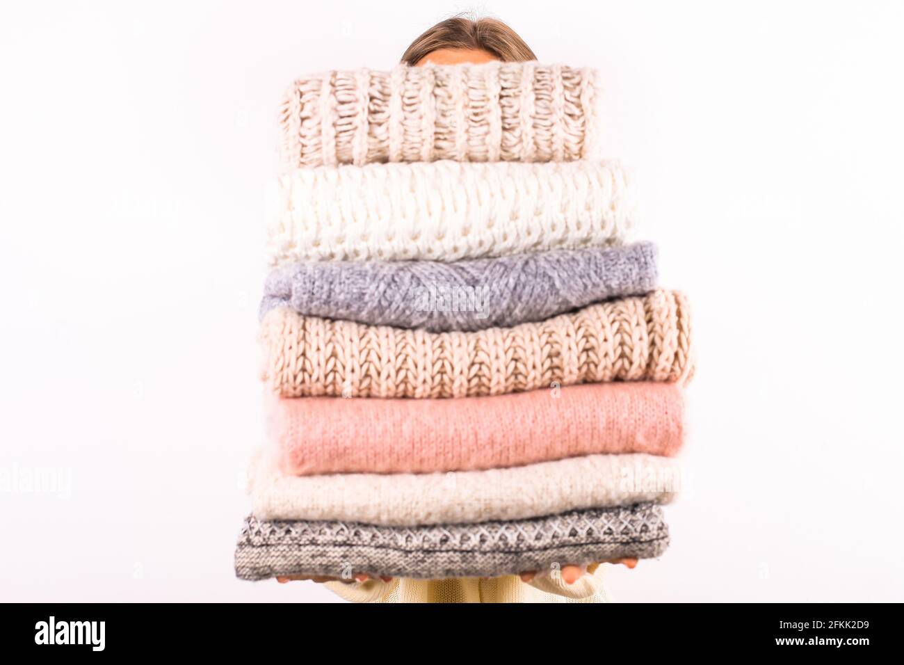 Close up of young woman holding huge stack of folded knitted warm ...