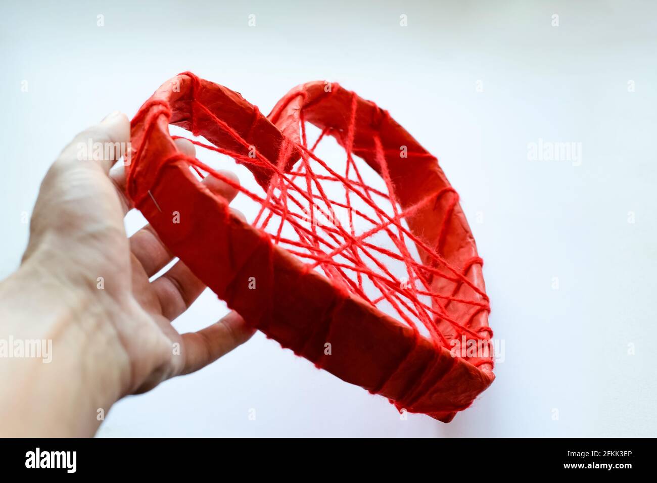 Heart made of cardboard and with red threads in a man's hand. A paper ...
