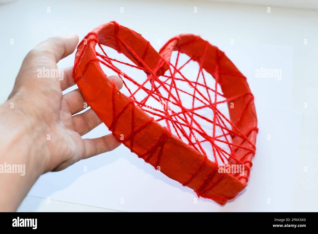 Heart made of cardboard and with red threads in a man's hand. A paper ...