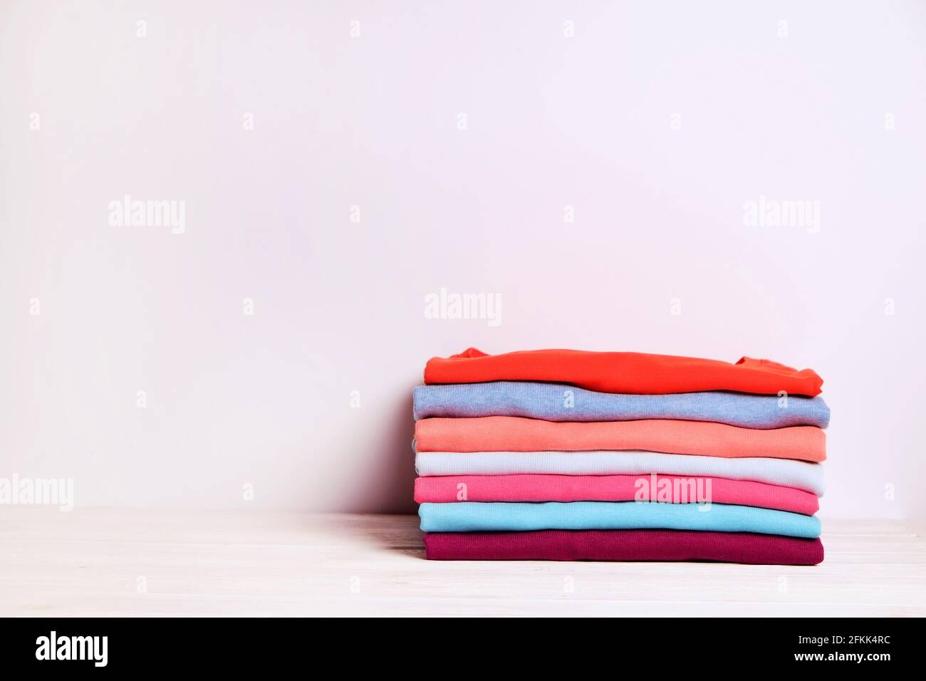 Stack of colorful perfectly folded t-shirts on white wooden texture ...