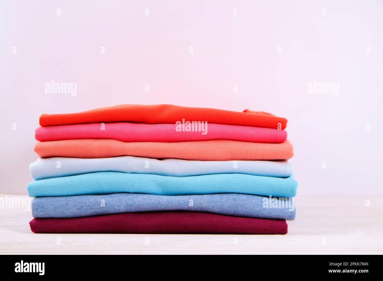 Stack of colorful perfectly folded t-shirts on white wooden texture ...