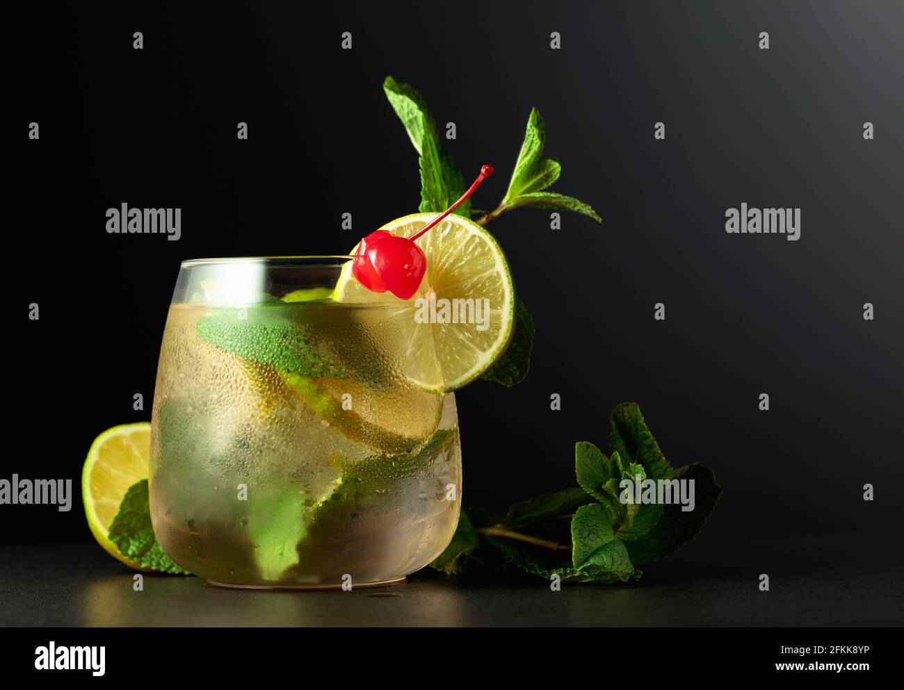 Cold refreshing drink with lime slices, mint, and cherry. Frozen glass ...