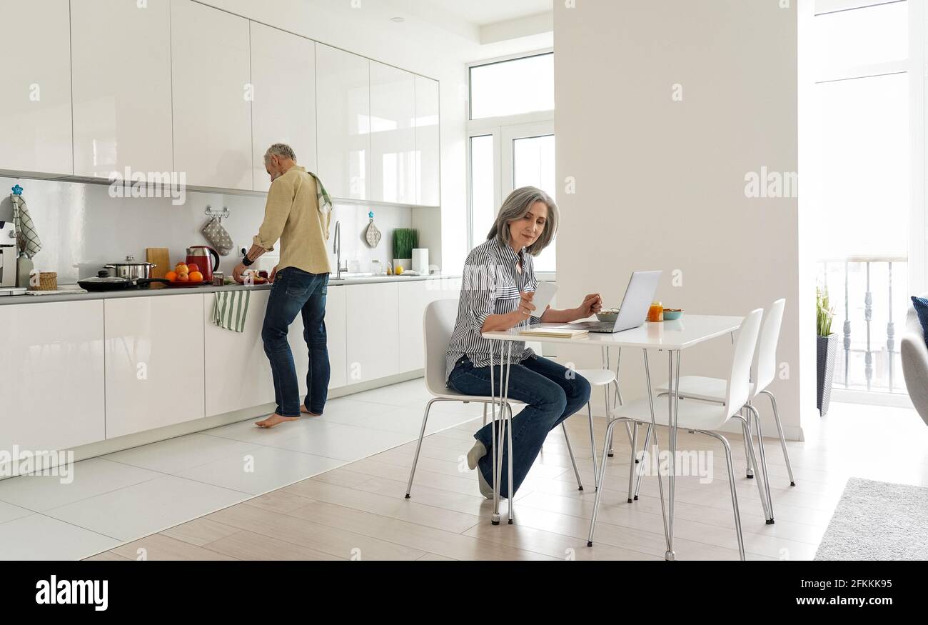 Mature wife remote working from home office while husband cooking in ...