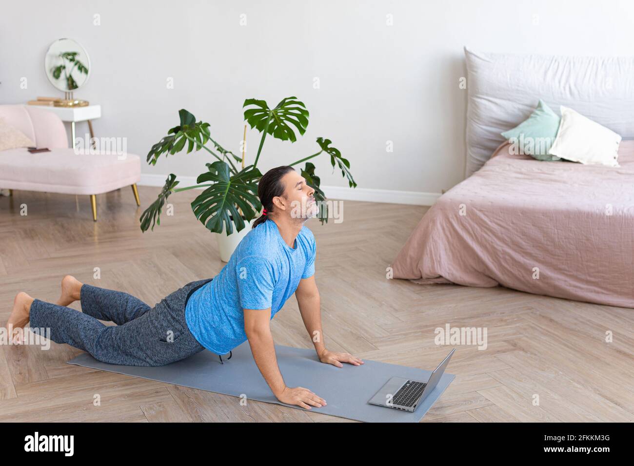 Health care concept - man practices yoga at home in front of a laptop ...